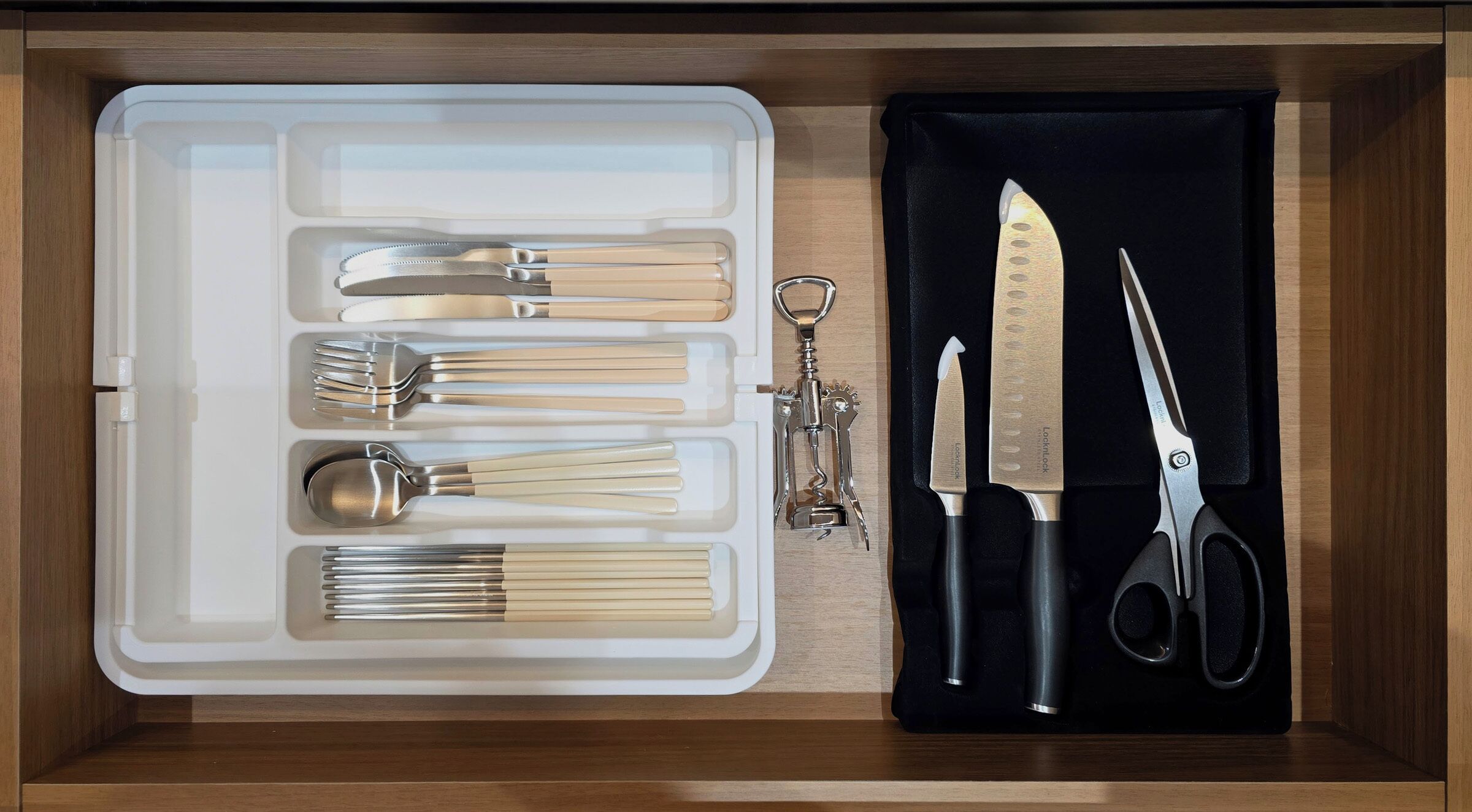 Uma gaveta com um conjunto de facas, abridor de garrafa e diversos utensílios.