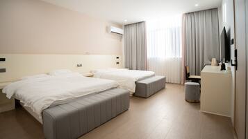 Quarto de hotel com duas camas, uma escrivaninha, uma cadeira, ar condicionado e televisão.