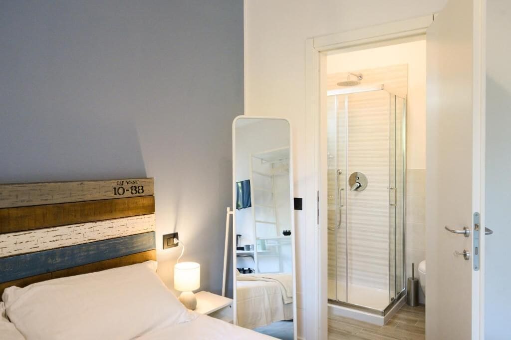 Quarto de hotel com cama, mesa de cabeceira, espelho e área de chuveiro.