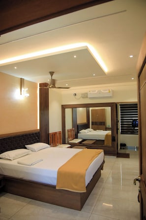 Quarto de hotel com uma cama grande, um ventilador de teto, aparelho de ar condicionado e um espelho refletindo o quarto.