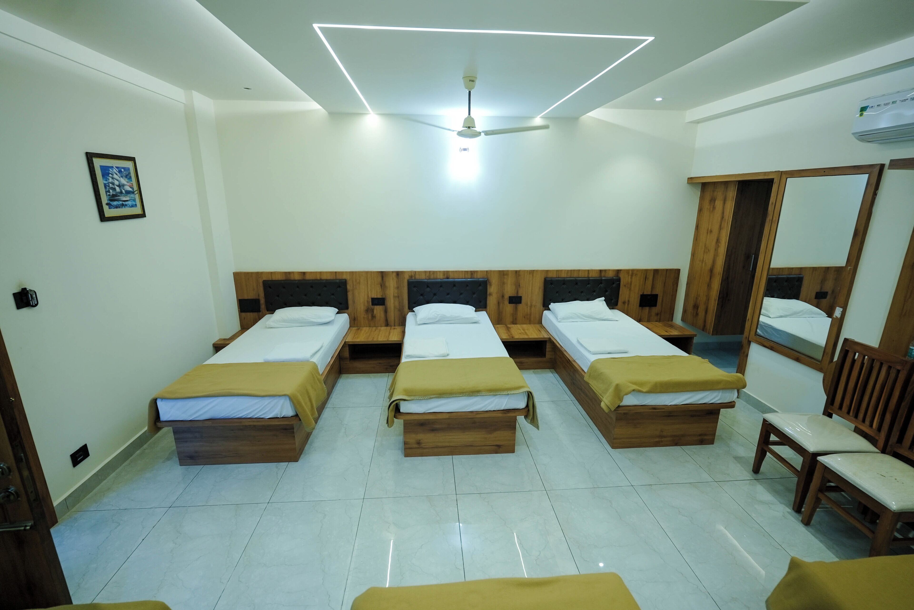 Quarto de hotel com quatro camas de solteiro, um ventilador de teto, um espelho grande e um guarda-roupa de madeira.