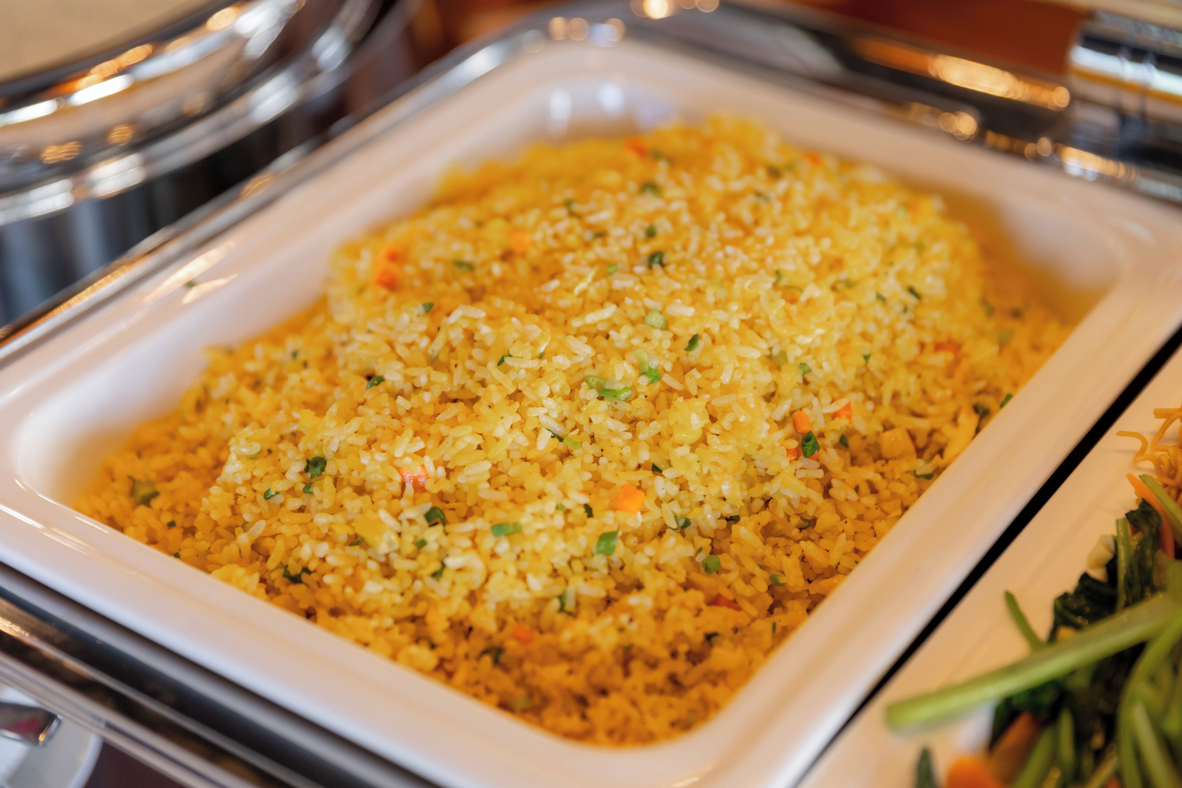 Uma travessa retangular branca cheia de arroz amarelo, decorada com ervas verdes e pequenos pedaços de legumes.
