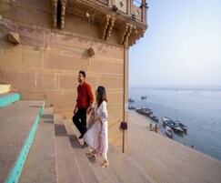 Um casal caminhando em uma escadaria de pedra com vista para um corpo de água e barcos.