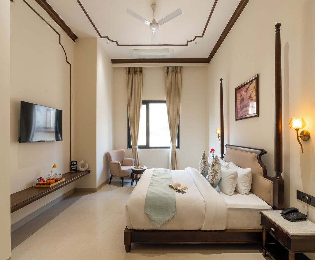 Quarto de hotel com uma cama grande, televisão de tela plana, mesa de cabeceira com abajur e ventilador de teto.