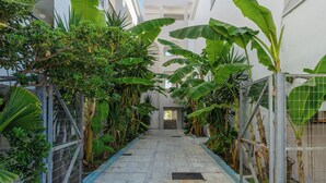 Corredor com cercas de metal e plantas verdes exuberantes, conduzindo a uma porta no final.