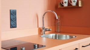 Cozinha moderna com pia de aço inoxidável, fogão embutido e luminária fixada na parede.
