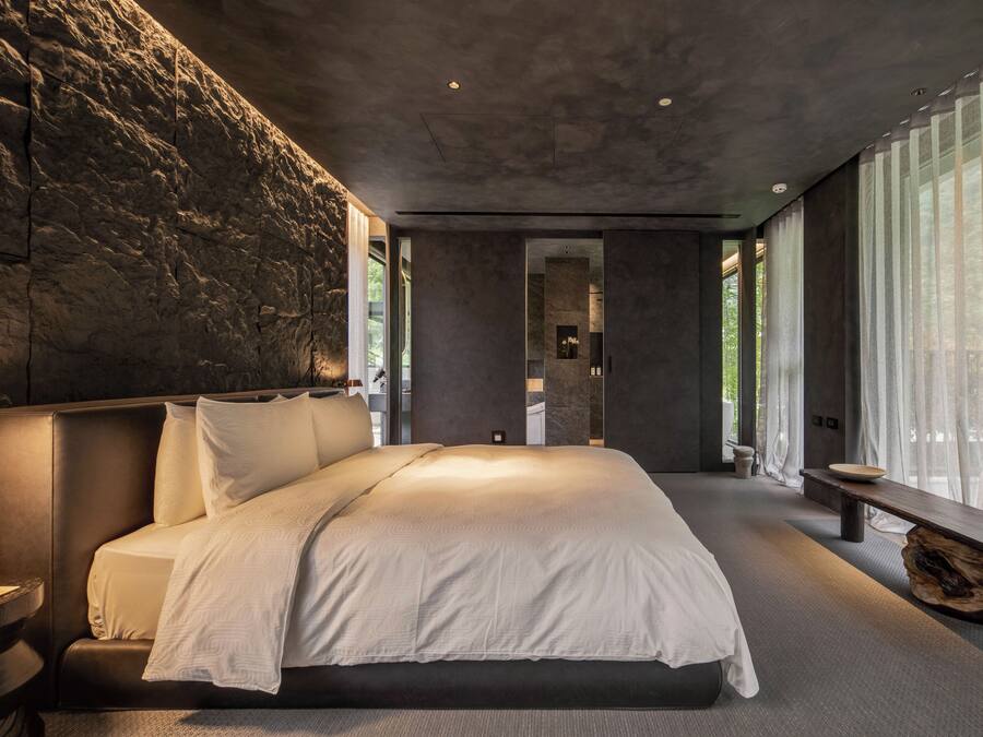 Quarto moderno com cama grande, parede de pedra e vista para um banheiro.