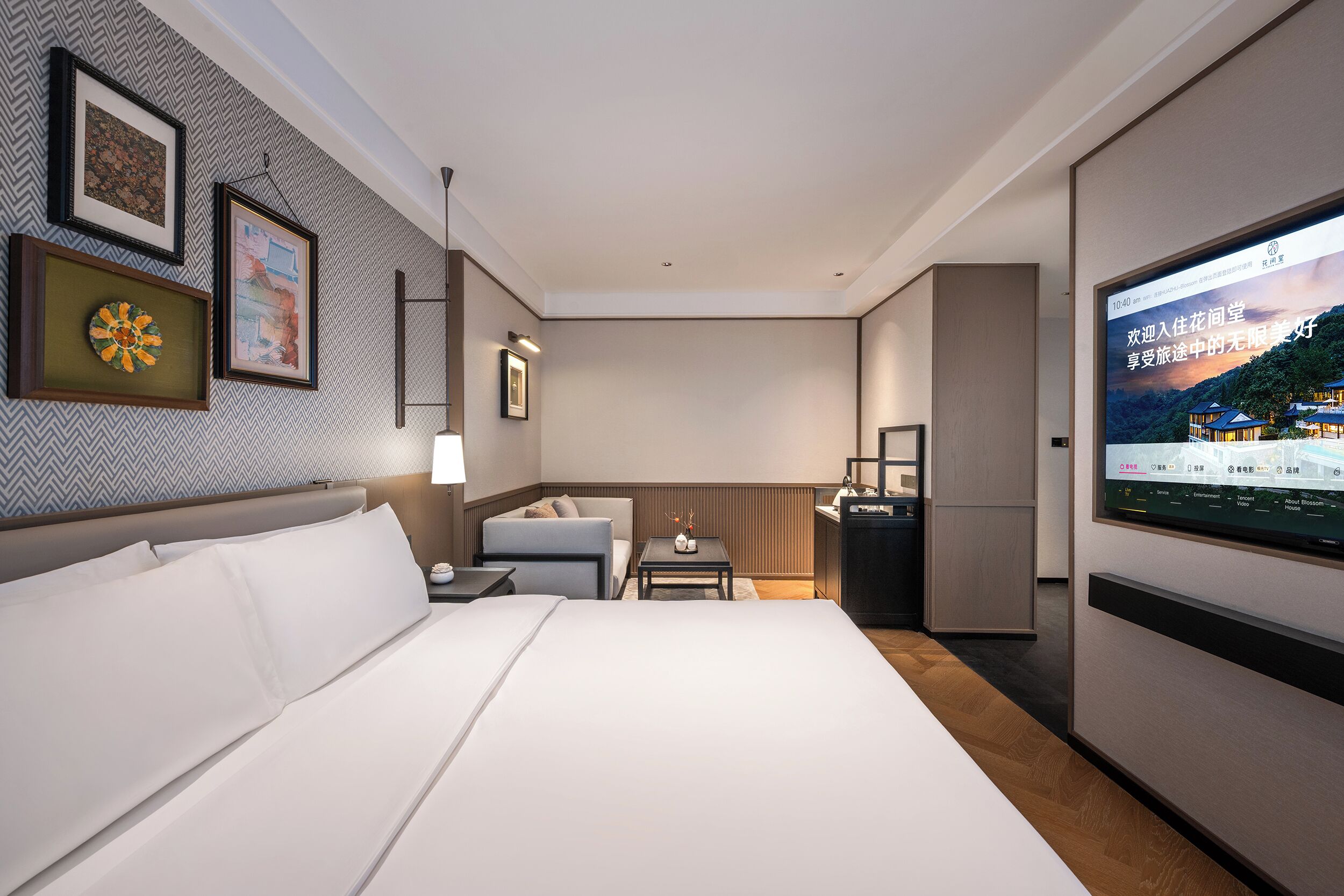 Quarto de hotel com cama, escrivaninha, televisão e parede com quadros.