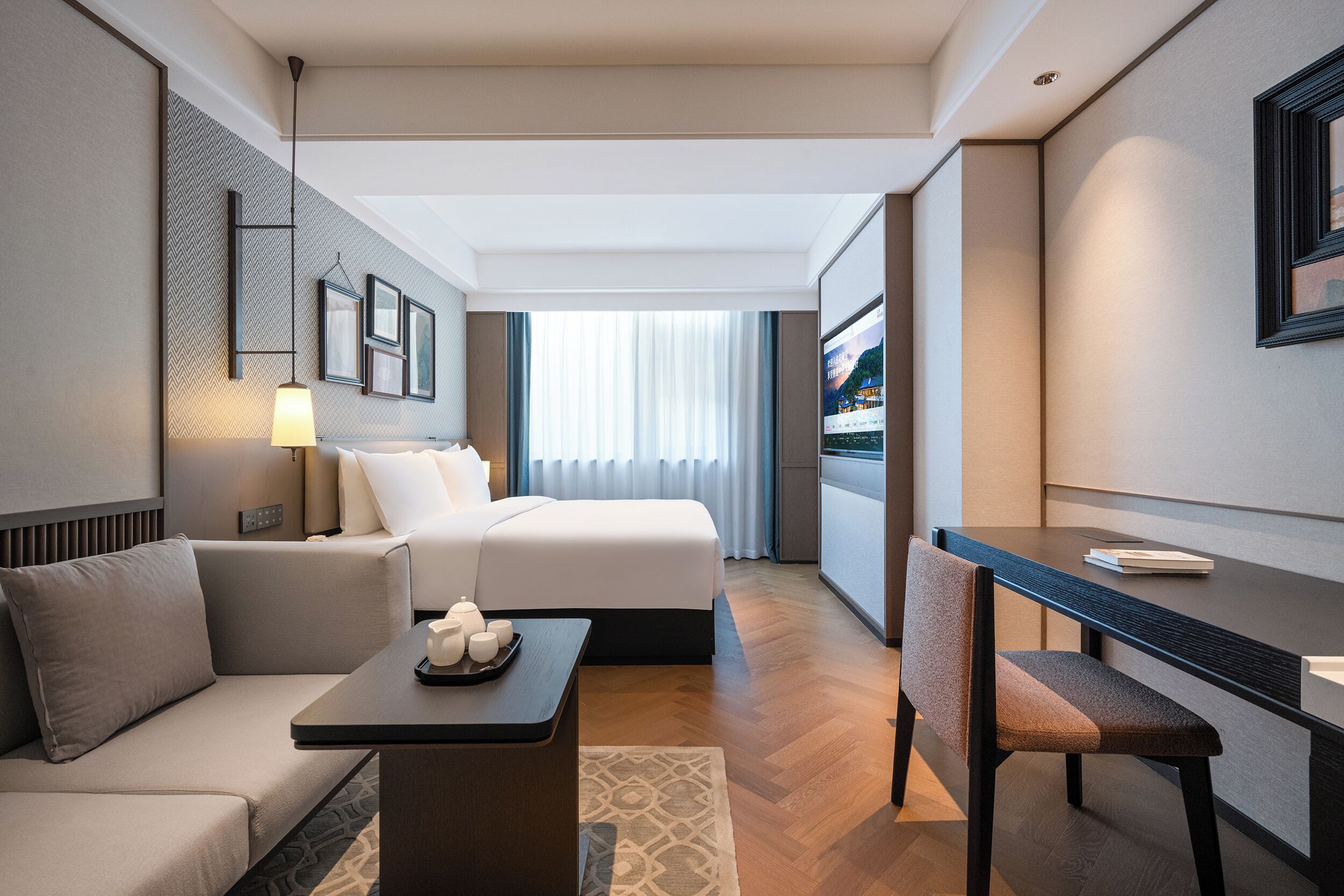 Quarto de hotel moderno com cama, sofá, escrivaninha e vista para a cidade.