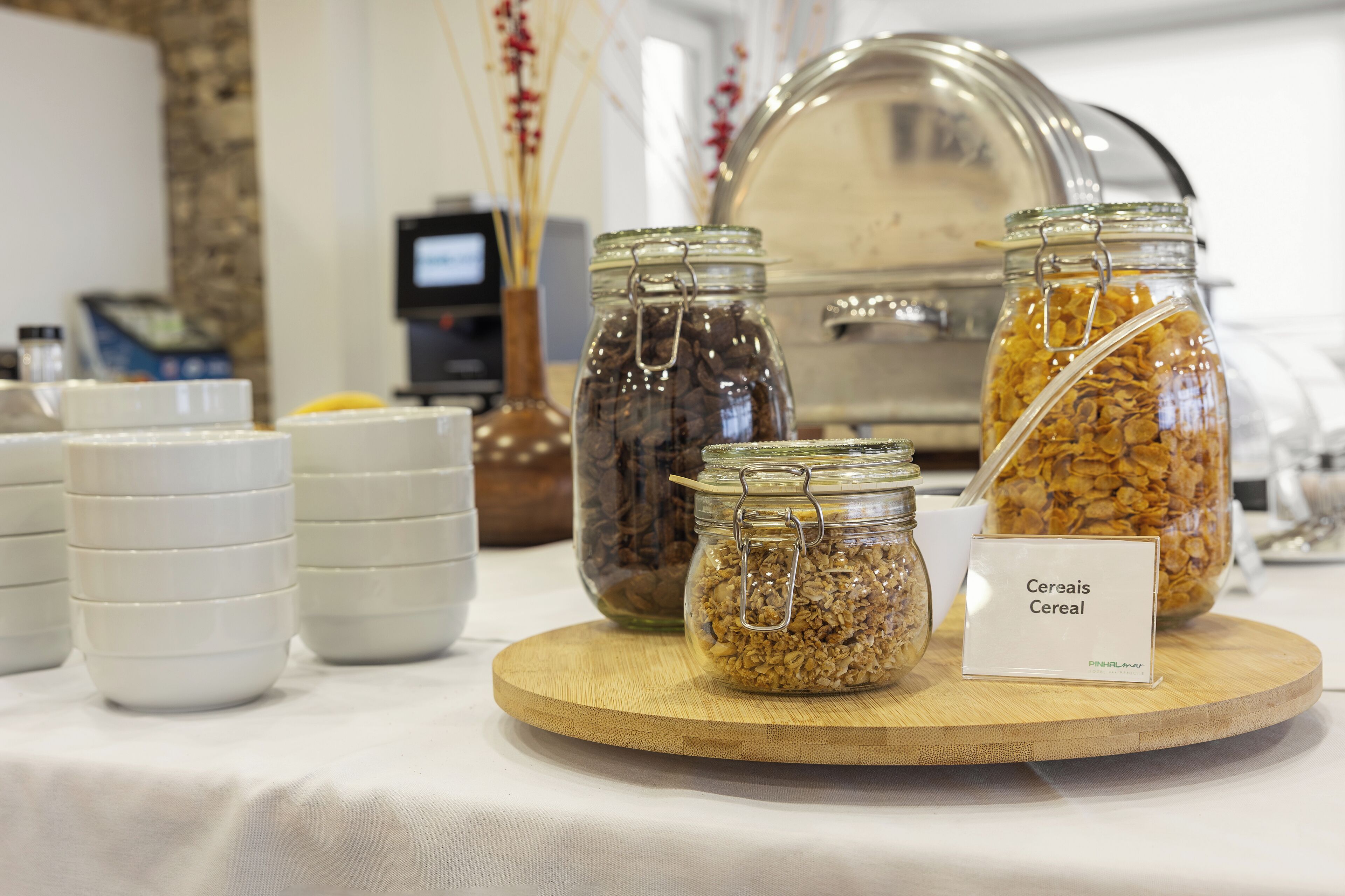 Buffet de café da manhã com diversas opções de cereais expostas em potes e tigelas.