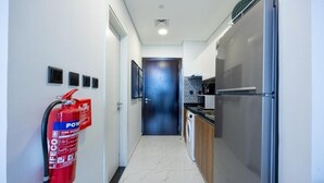 Um corredor estreito com um extintor preso na parede, uma porta no final e um frigorífico à direita.