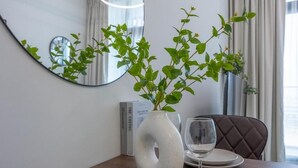 Mesa de jantar com um vaso branco contendo plantas verdes, uma taça de vinho e um livro intitulado "The Cotton".