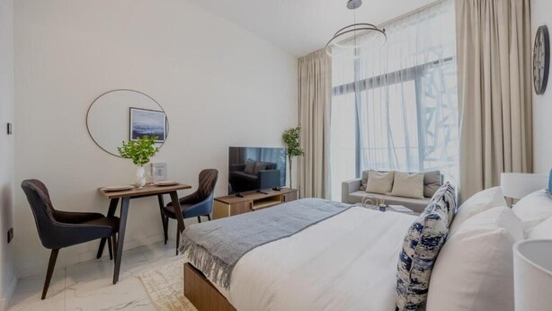 Quarto de hotel moderno com uma cama grande, uma escrivaninha com cadeira, televisão e um sofá.