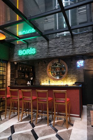 Uma área de bar com letreiros de neon, um espelho redondo e banquetas vermelhas.