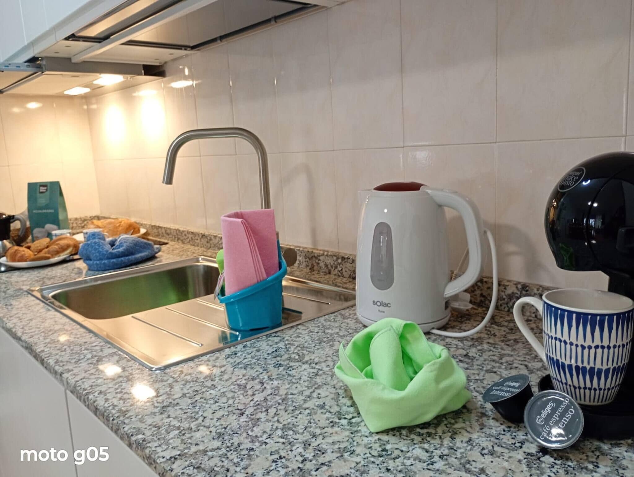 Cozinha com bancada de granito, chaleira branca, cafeteira e pia.