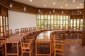 Uma sala de conferências com mesas e cadeiras de madeira, janelas amplas e um quadro branco.