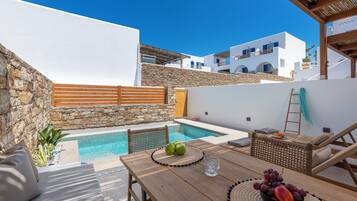 Uma área à beira da piscina com uma mesa de madeira, cadeiras de lounge e uma parede de pedra.