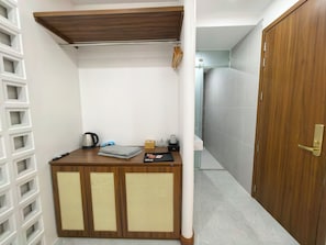 Quarto compacto com uma secretária de madeira, chaleira, caixa de lenços e uma pequena estante.