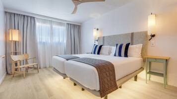 Quarto de hotel moderno com uma cama grande, duas mesas de cabeceira, um ventilador de teto e vista para o exterior através de grandes janelas.