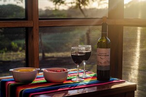 Uma garrafa de vinho, duas taças e duas tigelas sobre uma mesa junto a uma janela.