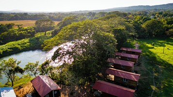 Vista para o rio de uma pousada com várias cabanas, cercada por vegetação exuberante e um rio.
