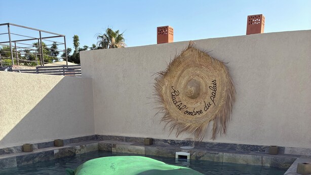 Piscina com capa verde, parede decorativa com padrão trançado e céu azul límpido.
