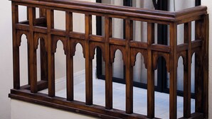 Varanda de madeira com guarda-corpo, janela com cortinas e uma porta.