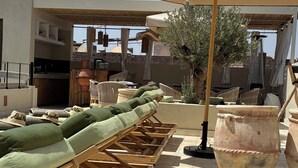 Terraço no telhado com cadeiras de descanso, um vaso grande e uma pérgola com guarda-sóis.