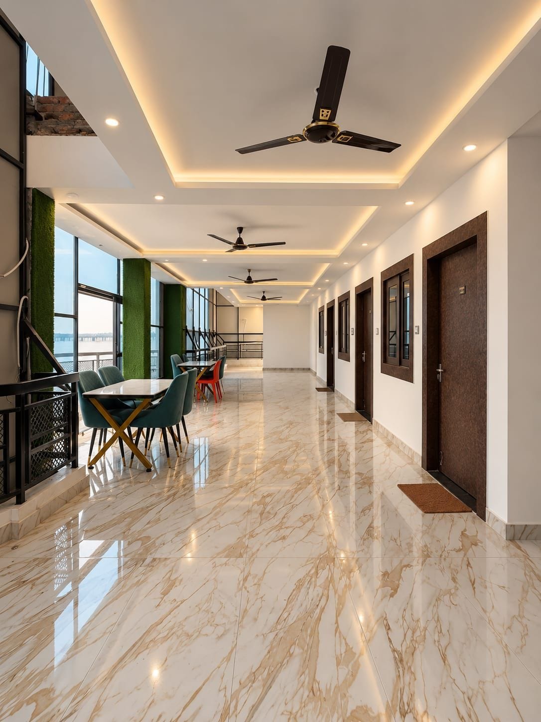 Um hall de hotel espaçoso, com piso de mármore, várias ventoinhas no teto e vista para uma ponte através de grandes janelas.