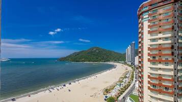 Paisagem costeira com praia, colina com edifícios e um hotel alto.