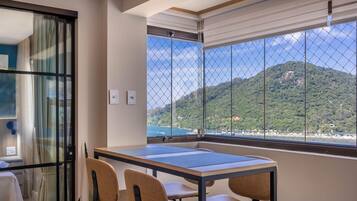 Quarto com mesa, cadeiras, janela e vista para paisagem montanhosa, além de porta de vidro.