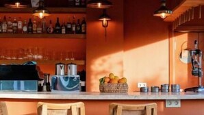 Uma área de bar com cadeiras de madeira, balcão com garrafas e luminárias pendentes.