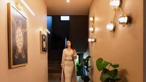 Corredor com uma mulher caminhando, iluminação embutida e luminárias fixadas na parede.