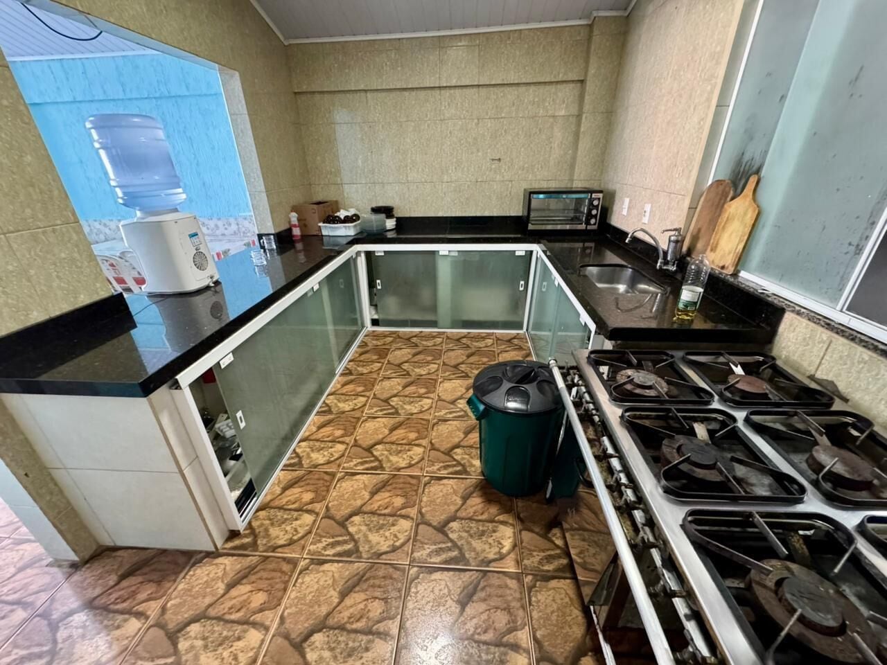 Cozinha com fogão a gás, bebedouro e lixeira.