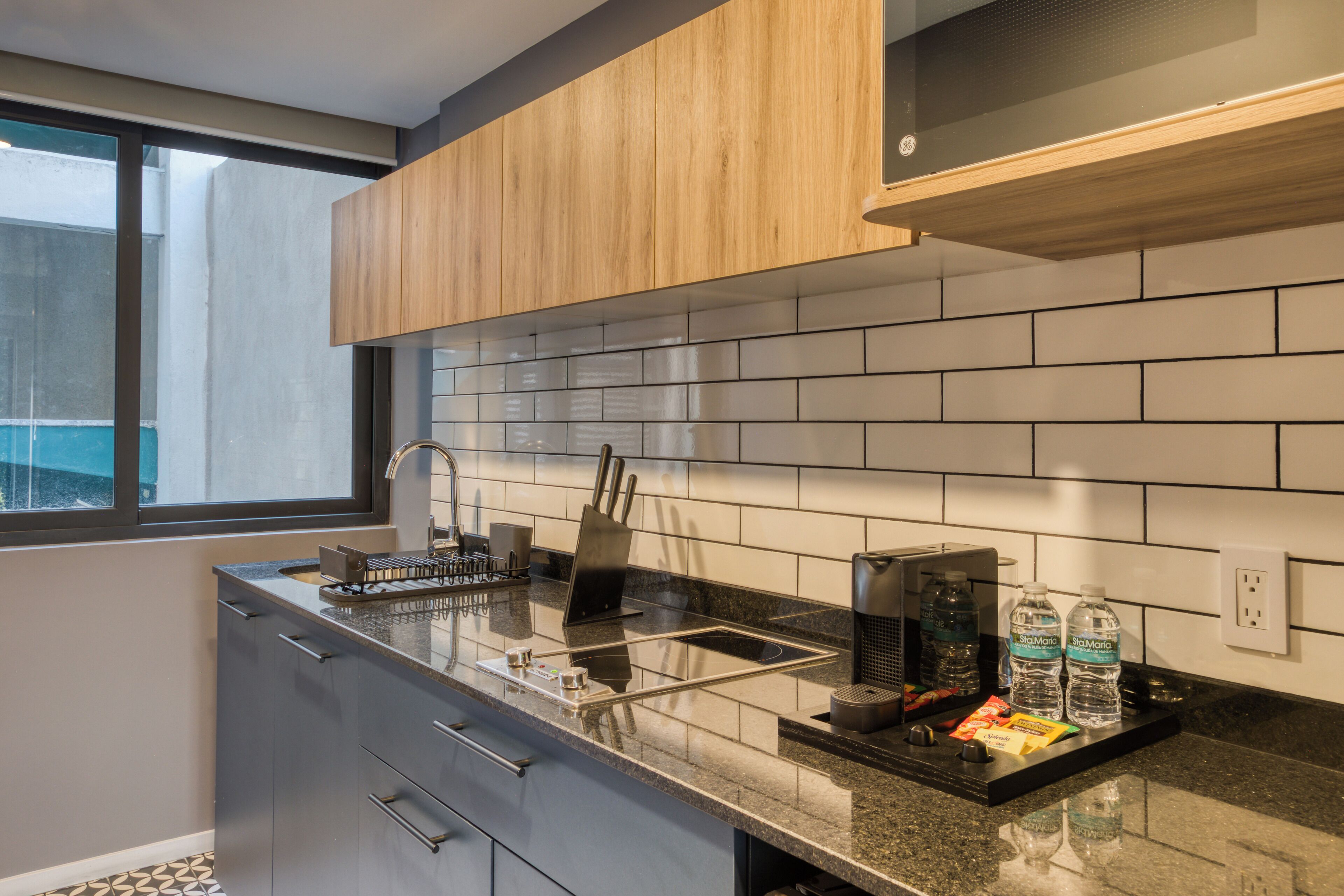Uma cozinha moderna com bancada de granito, armários de madeira e painel de fundo preto.