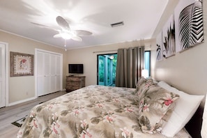 Quarto com cama, ventoinha no teto, obras de arte e vista para o verde lá fora.