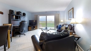 Sala de estar com televisão, sofá de couro e área de jantar com mesa e cadeiras.