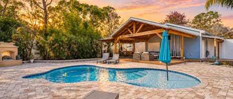 Piscina com área de estar rebaixada, rodeada por um pátio com espreguiçadeiras e um espaço de estar coberto ao ar livre.