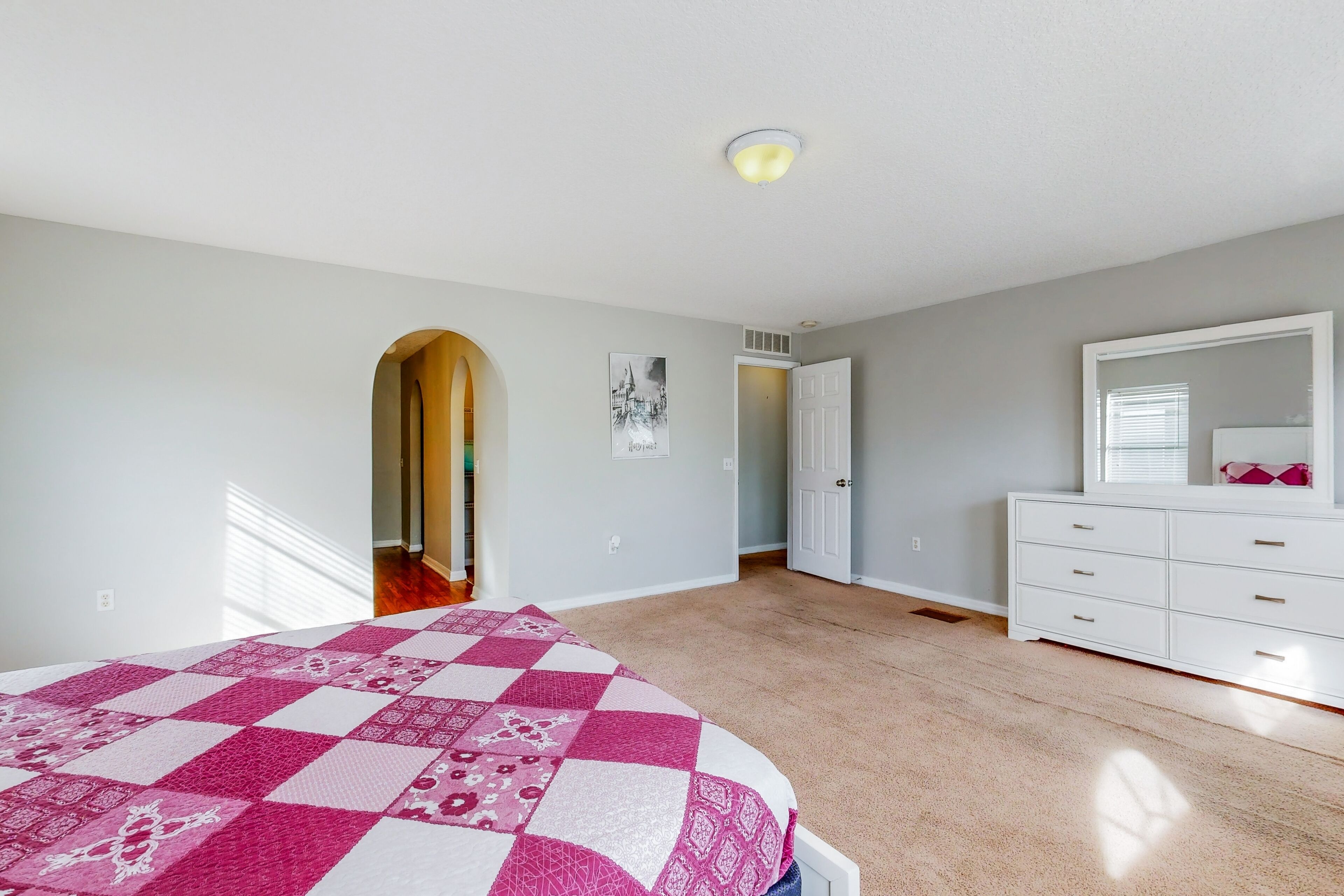 Um quarto com uma cama, cômoda, porta e corredor.