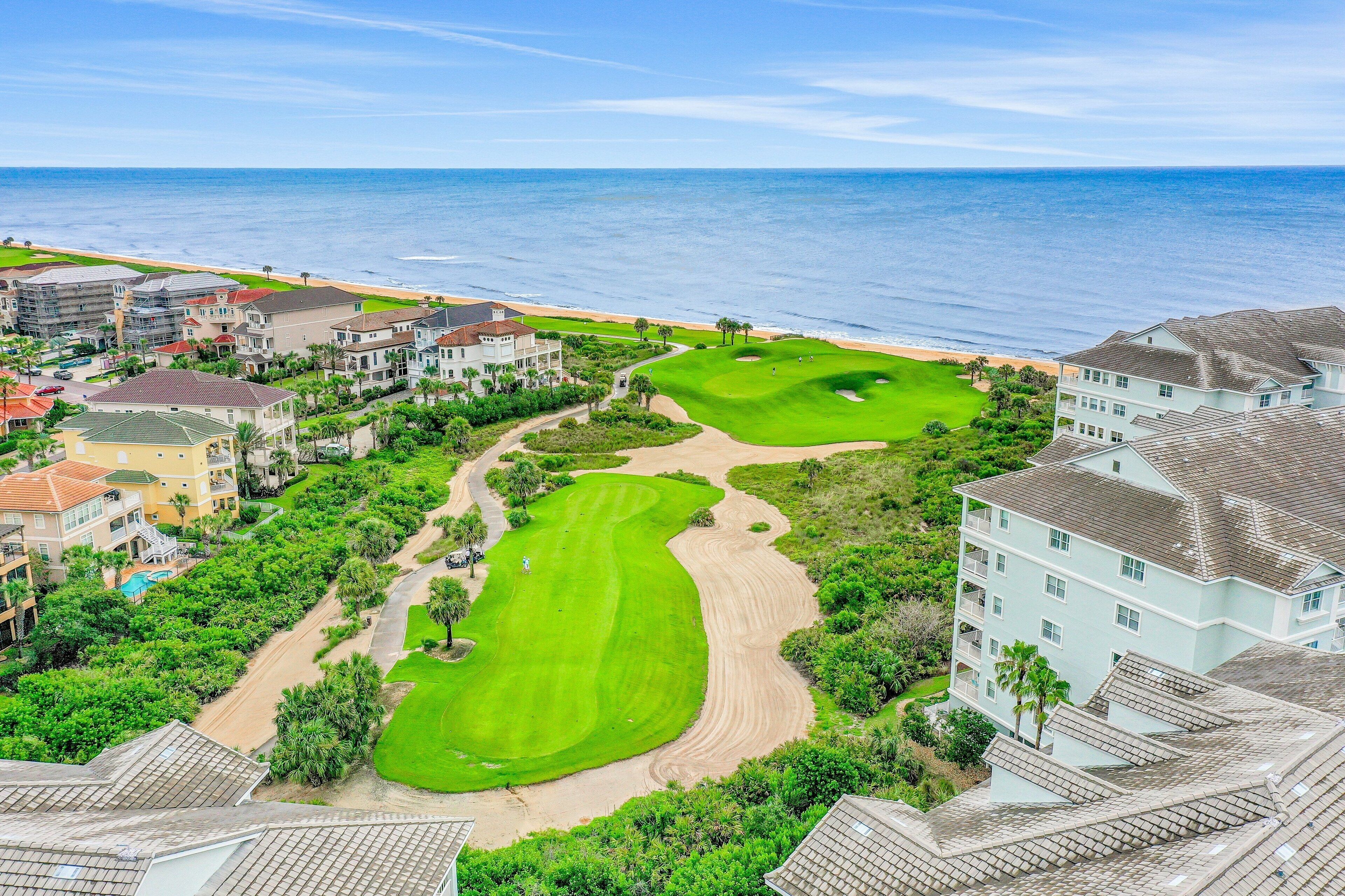 Campo de golfe com vista para o oceano, rodeado por edifícios residenciais.