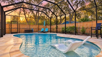 Piscina com borda curva, cercada por um deck de madeira e uma área coberta com cadeiras.