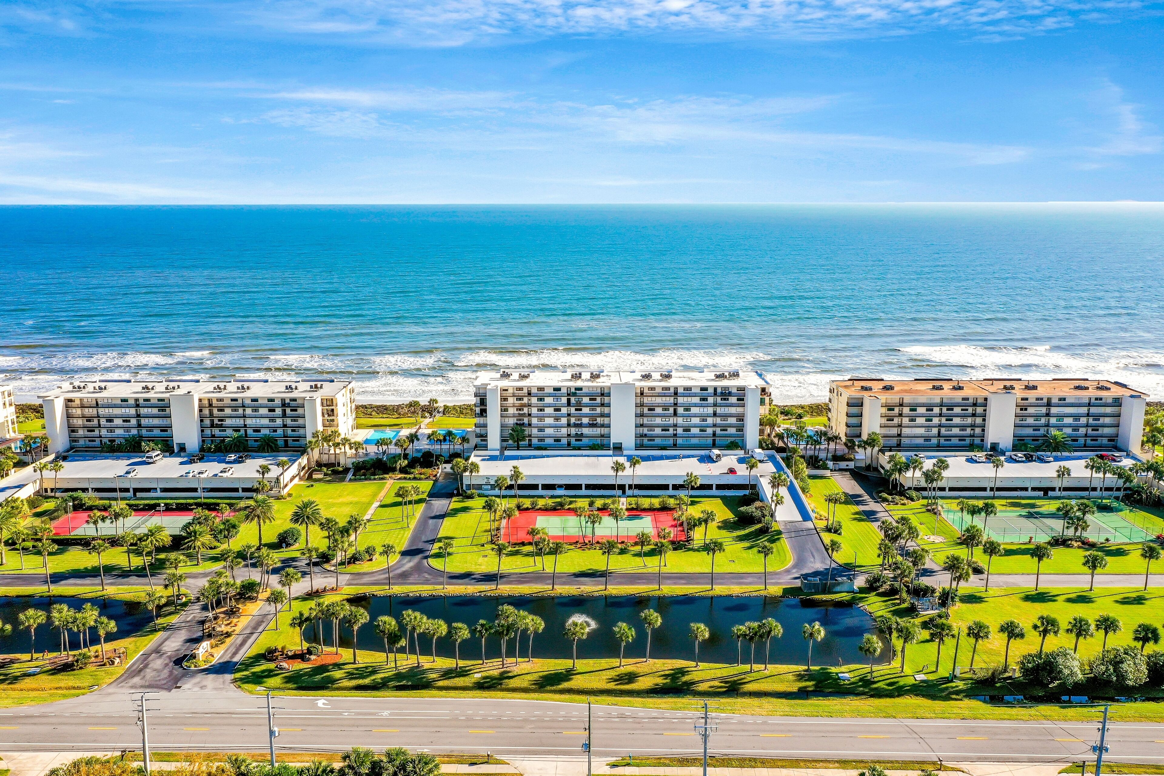 Hotel com vários edifícios, quadra desportiva e estrada que leva à praia.