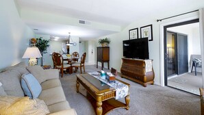 Sala de estar com sofá, mesa de centro, televisão e área de jantar com cadeiras e mesa.