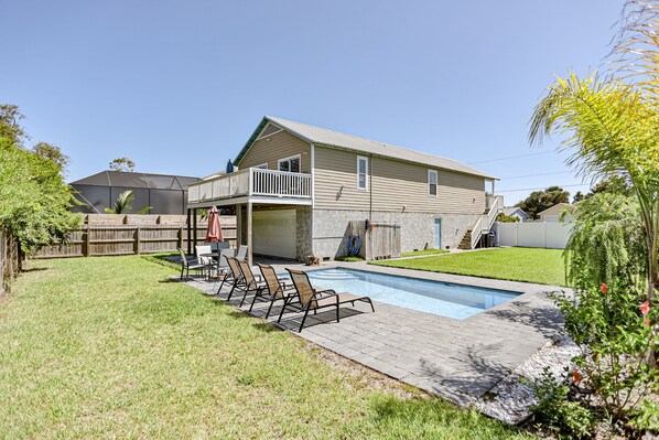Uma casa com piscina, um deck com cadeiras e um quintal cercado.