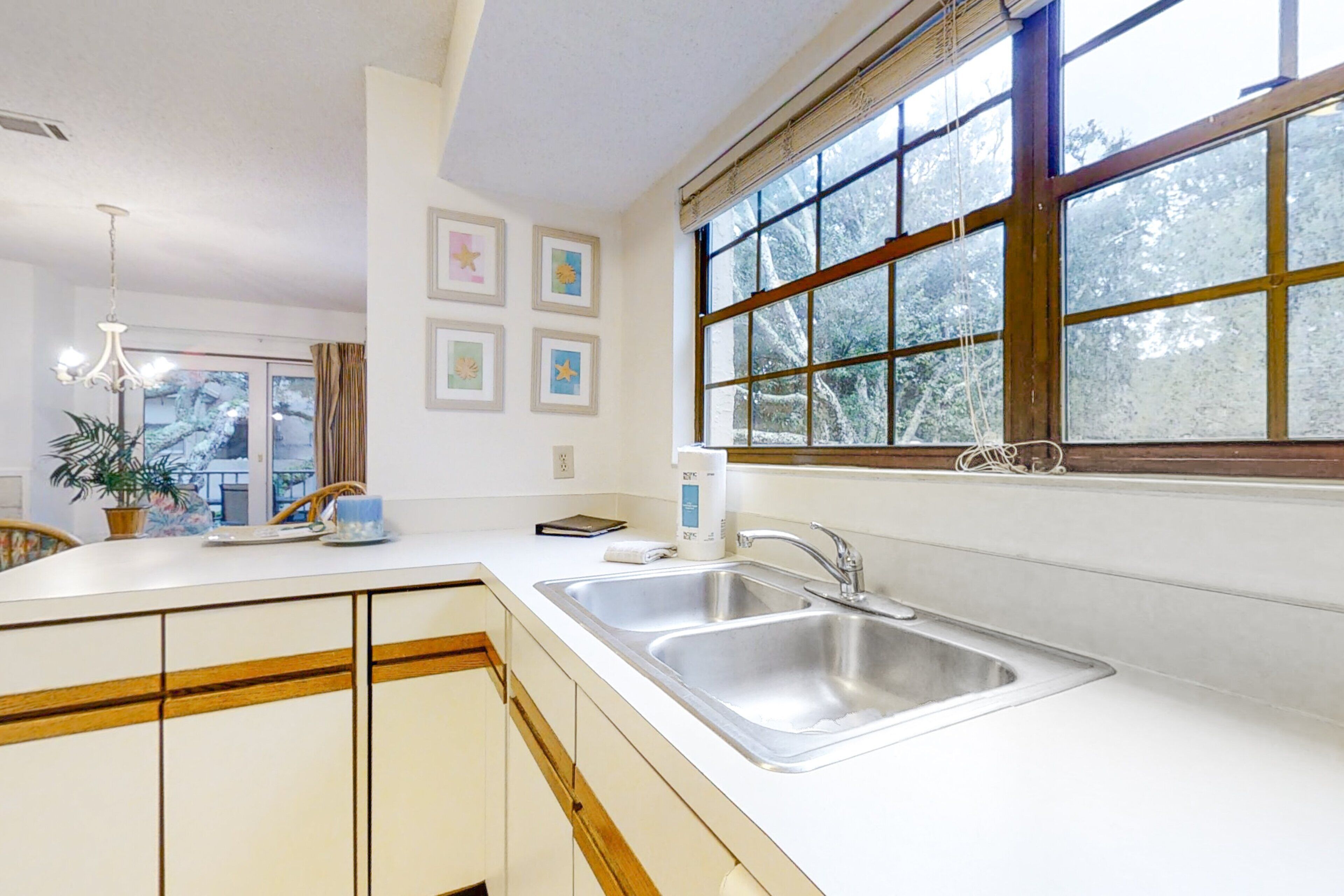 Uma cozinha com duas pias, uma janela com vista para árvores e quadros nas paredes.