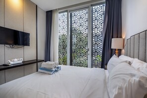 Quarto de hotel com cama, televisão na parede, abajur e janela com padrão geométrico.