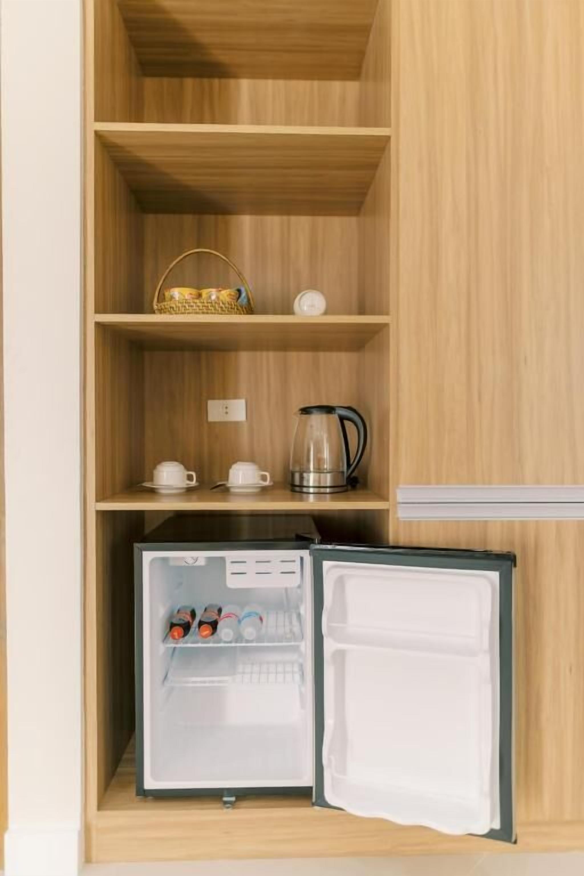 Uma geladeira compacta com compartimento para congelador, uma prateleira com cesta e copos, e uma chaleira na prateleira superior.