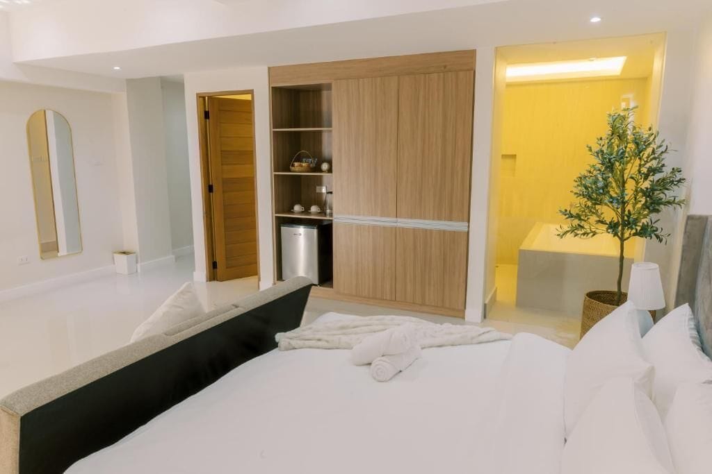 Quarto de hotel moderno com uma cama grande, um guarda-roupa de madeira, um banheiro pequeno e uma planta.