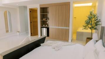 Quarto de hotel moderno com uma cama grande, um guarda-roupa de madeira, um banheiro pequeno e uma planta.