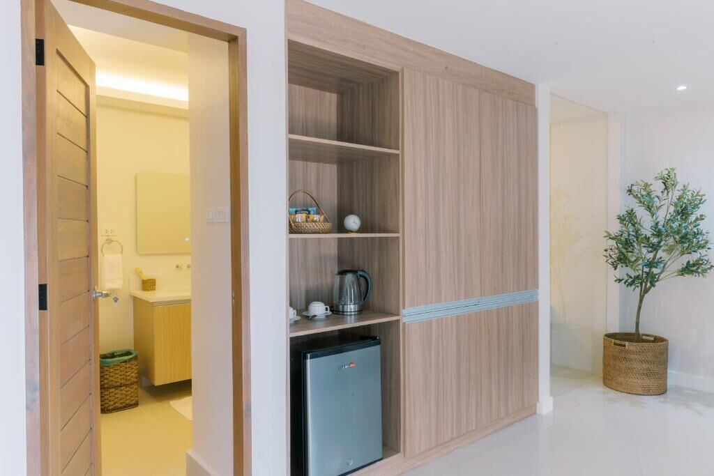 Quarto moderno com guarda-roupa embutido, pequeno frigorífico e planta em vaso.